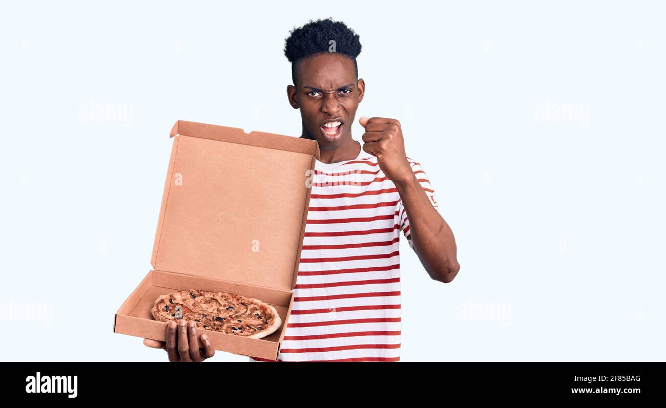 Young african american man holding delivery pizza box annoyed and ...