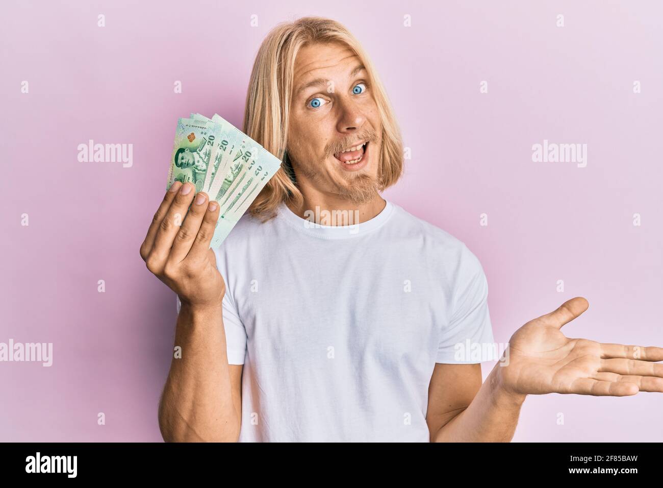 Caucasian young man with long hair holding 20 thai baht banknotes ...