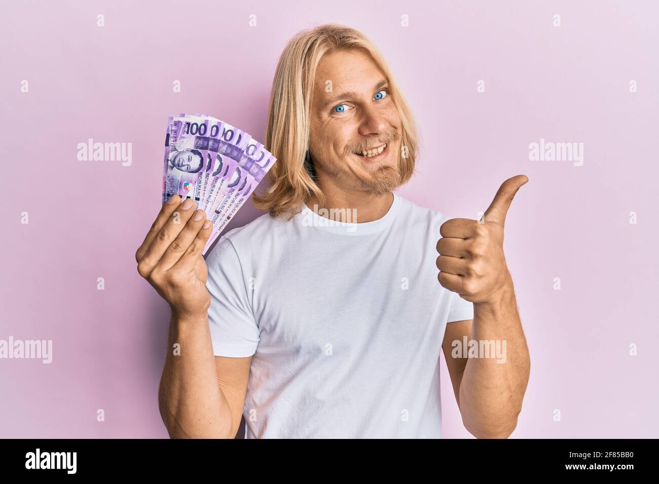 Caucasian young man with long hair holding 100 philippine peso ...