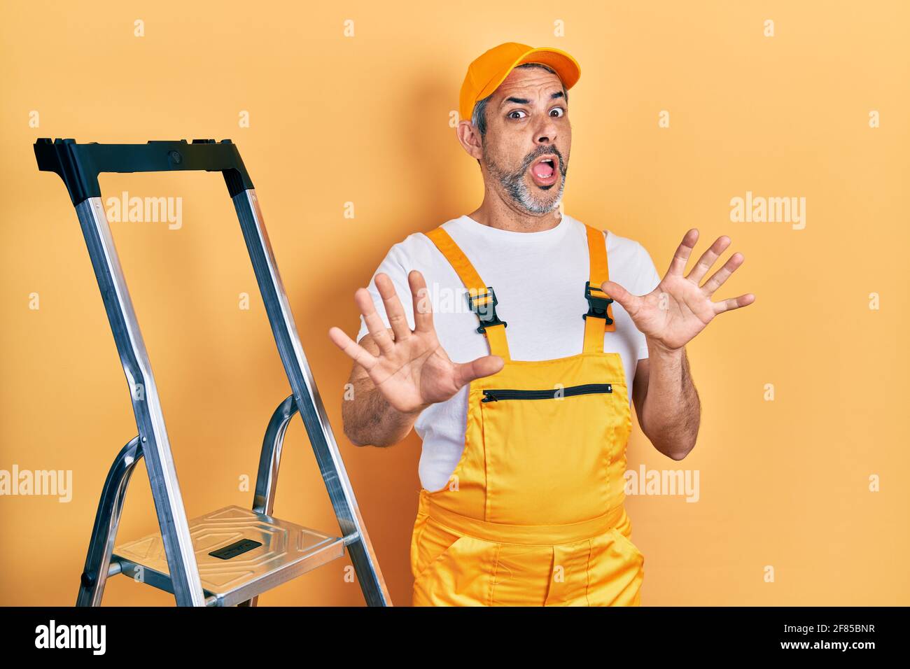 Handsome middle age man with grey hair holding ladder afraid and ...