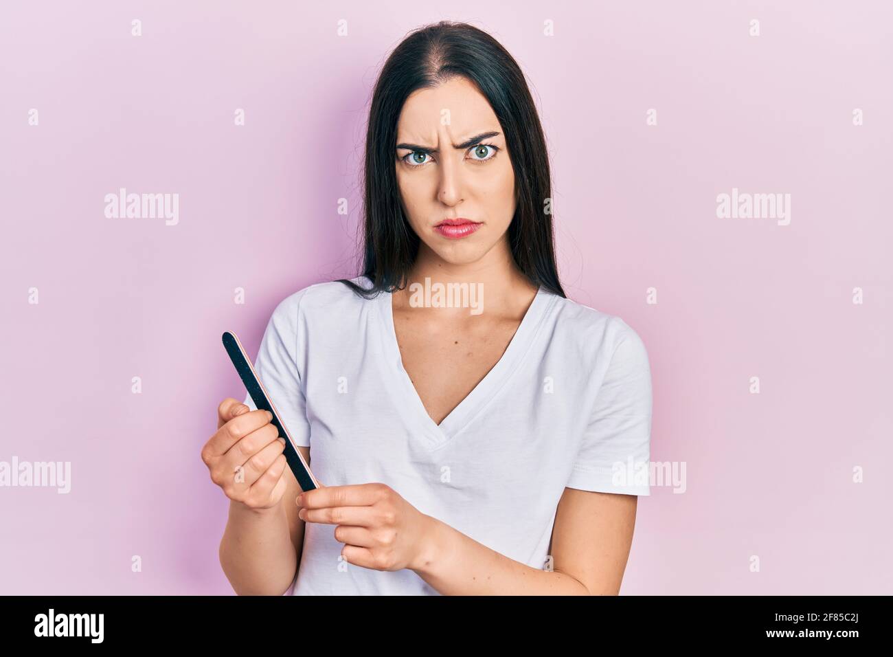 Beautiful woman with blue eyes using file nail skeptic and nervous ...