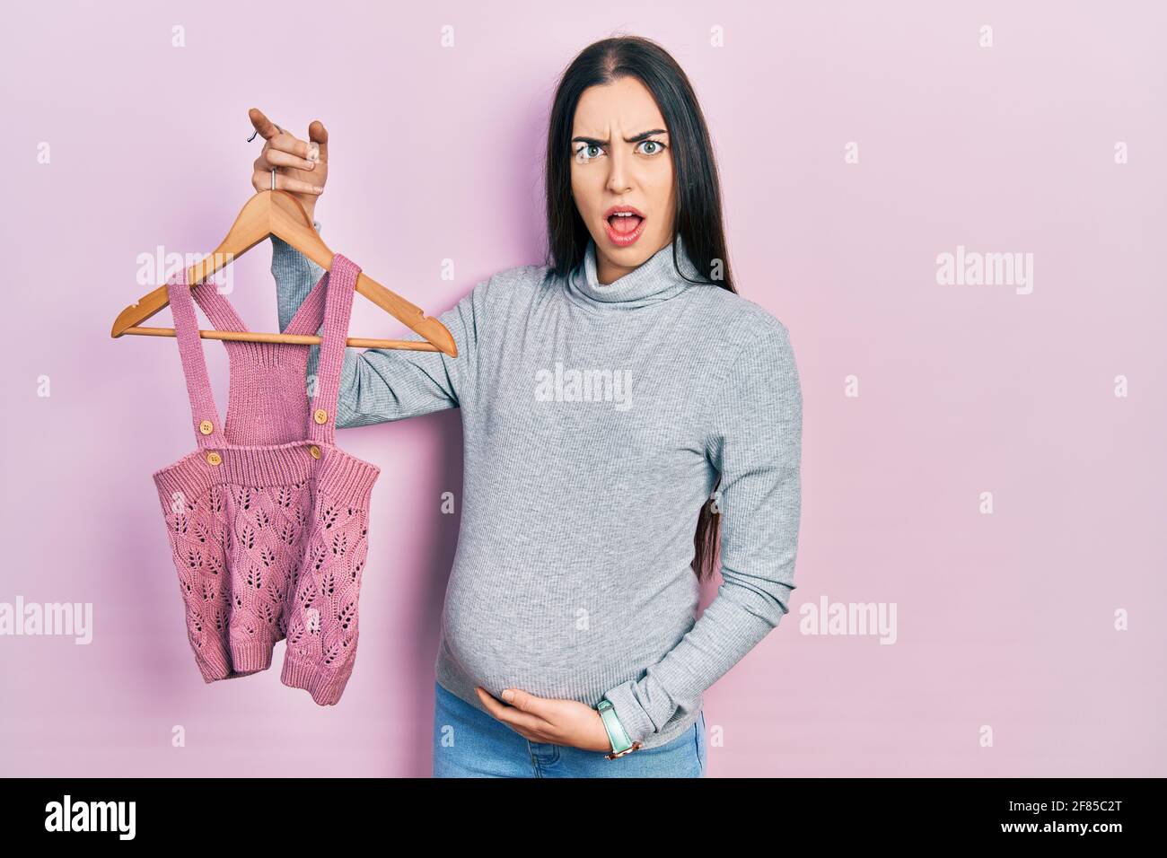 Beautiful woman with blue eyes expecting a baby holding baby clothes in ...