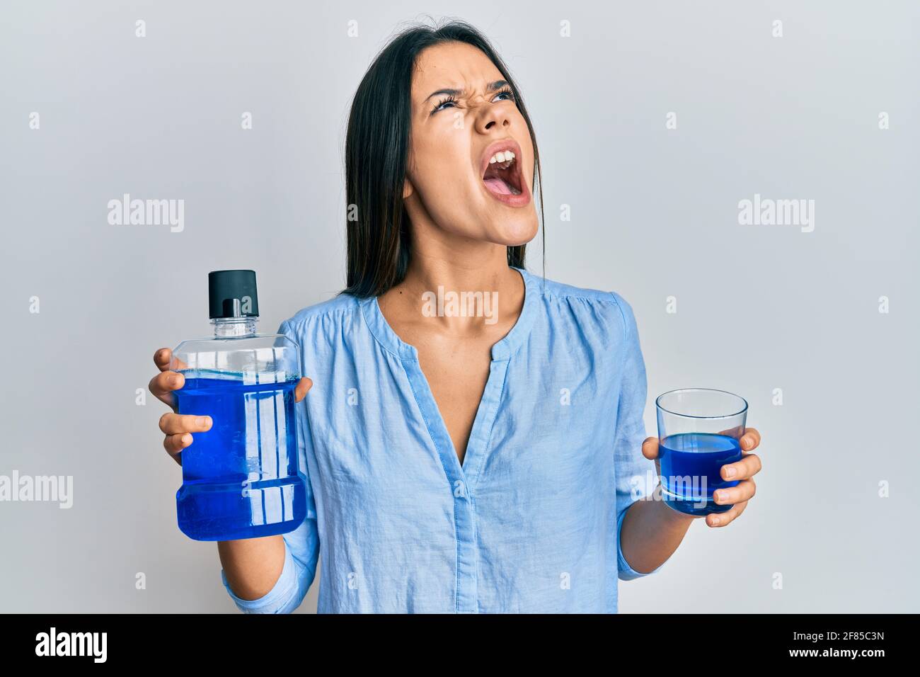 Young hispanic girl holding mouthwash for fresh breath angry and mad ...
