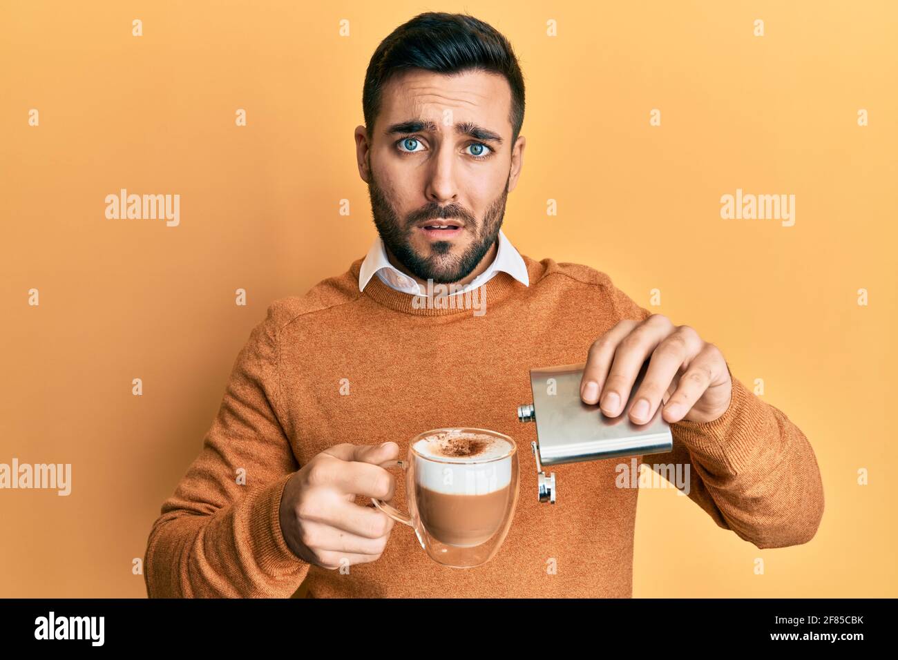 Young hispanic man drinking a cup of coffee with alcohol clueless and ...