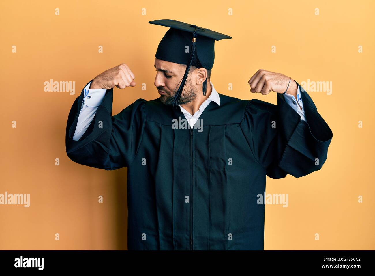 Young hispanic man wearing graduation cap and ceremony robe showing ...