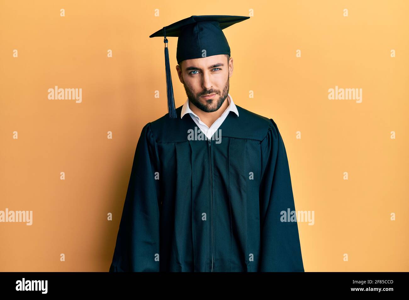 Young hispanic man wearing graduation cap and ceremony robe skeptic and ...