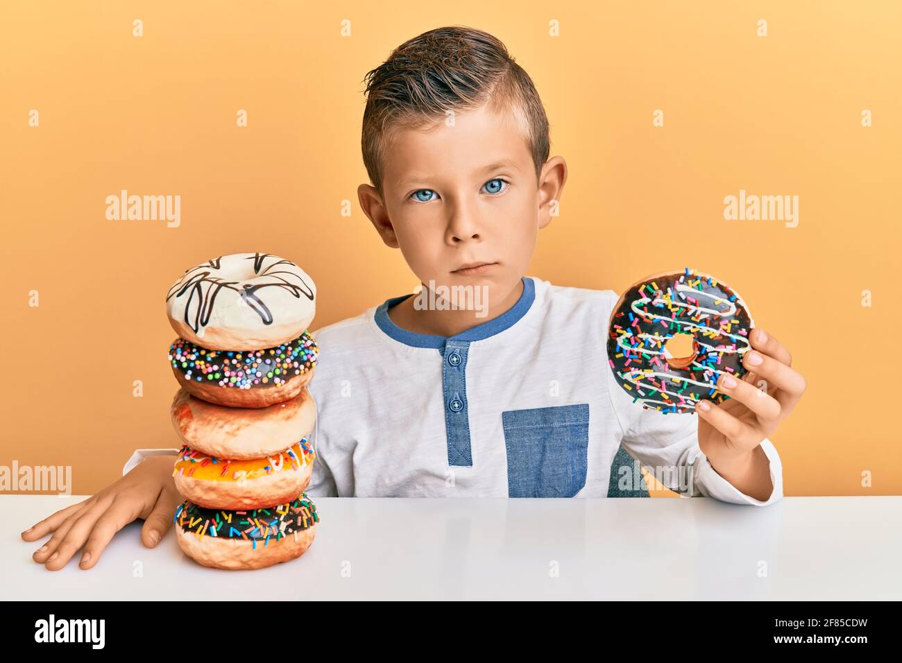 Adorable caucasian kid eating doughnuts for breakfast depressed and ...