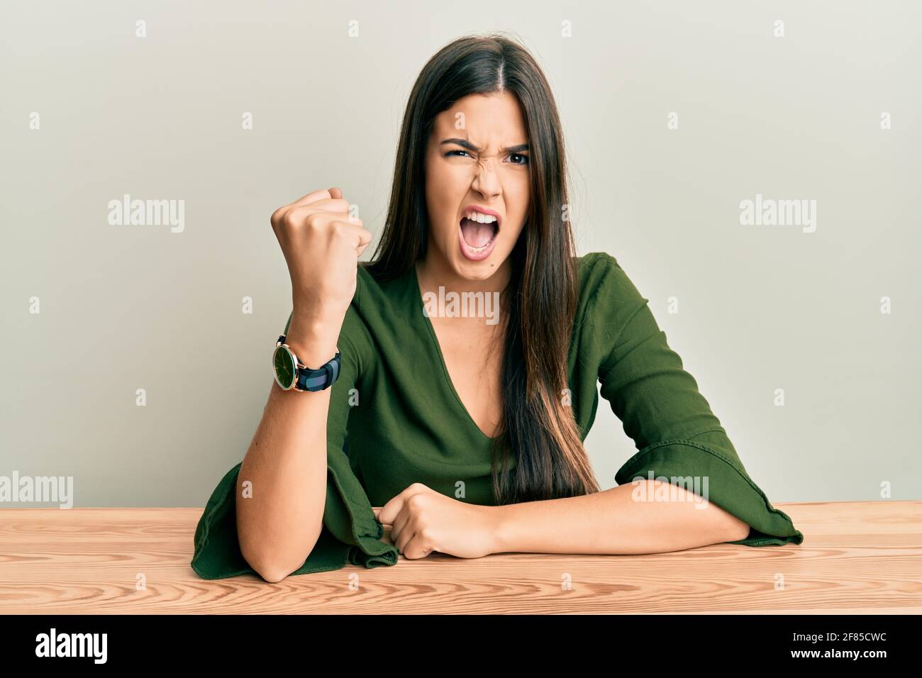 Young brunette woman wearing casual clothes sitting on the table angry ...
