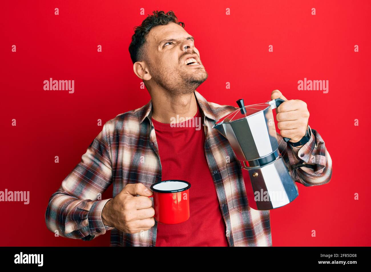 Young hispanic man drinking italian coffee angry and mad screaming ...
