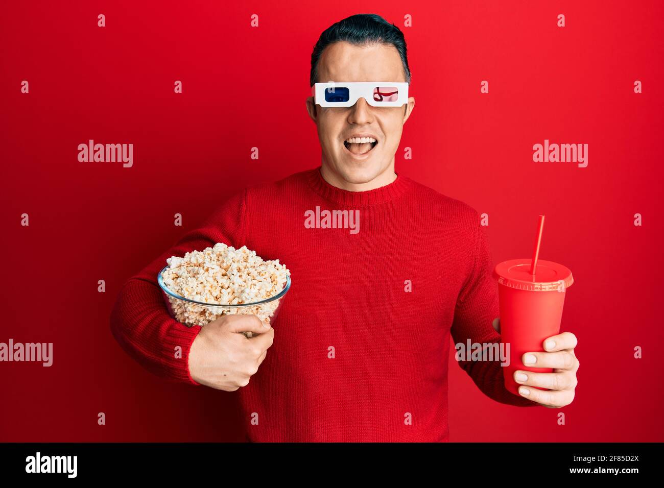 Handsome young man eating popcorn and soda wearing 3d glasses ...