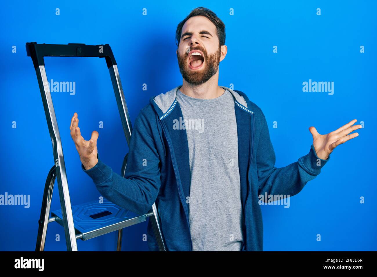 Caucasian man with beard by ladder crazy and mad shouting and yelling ...
