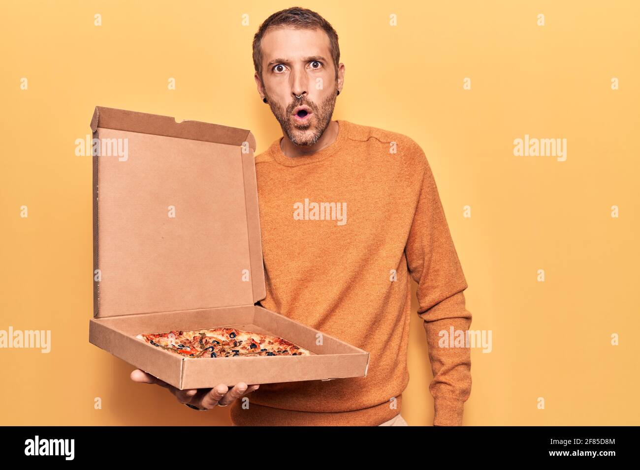 Young handsome man holding delivery pizza box scared and amazed with ...