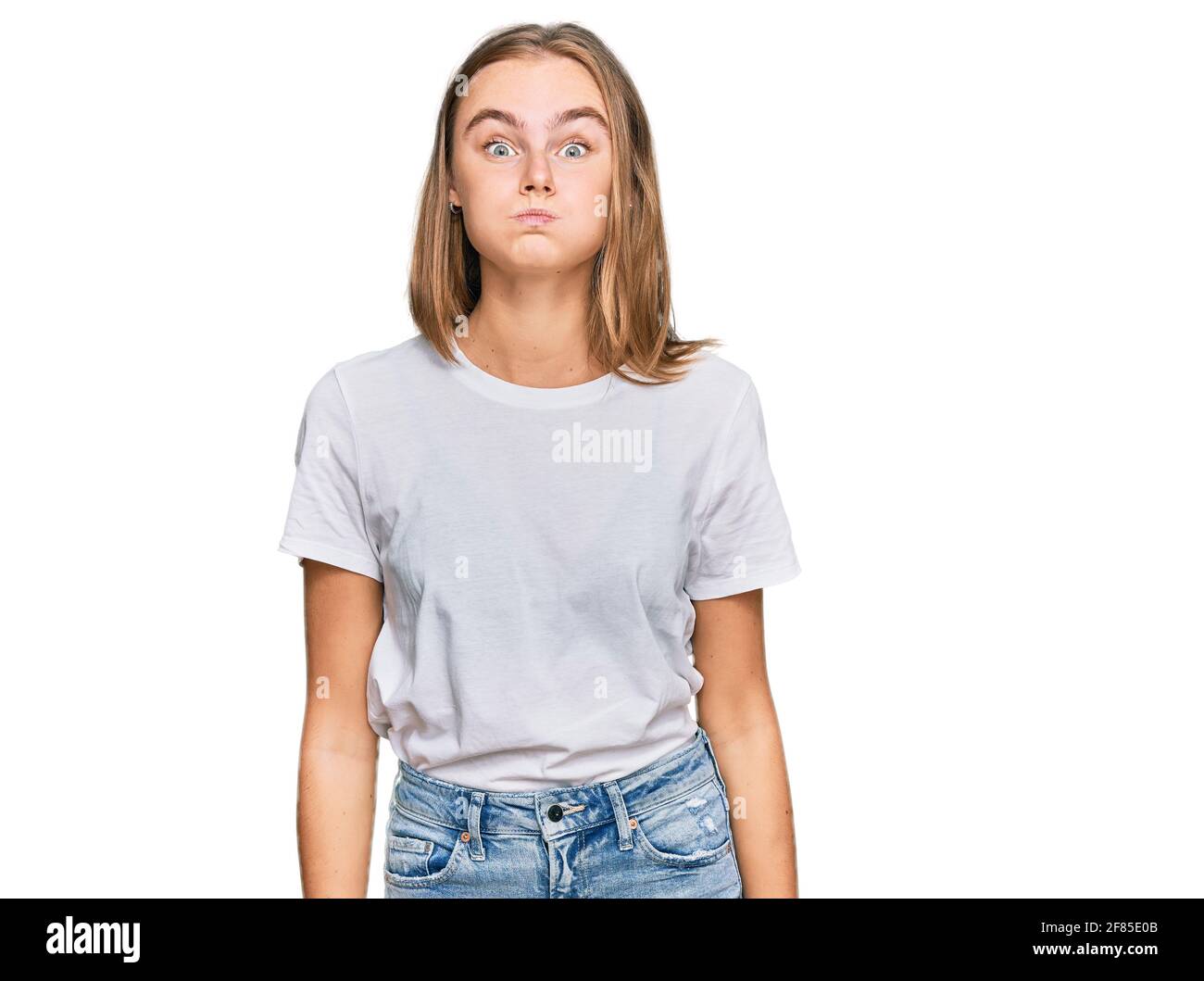 Beautiful young blonde woman wearing casual white t shirt puffing ...