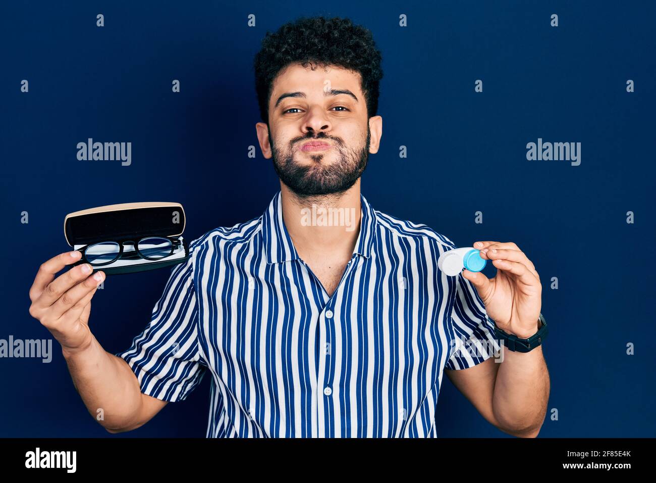 Young arab man with beard holding glasses and contact lenses puffing ...