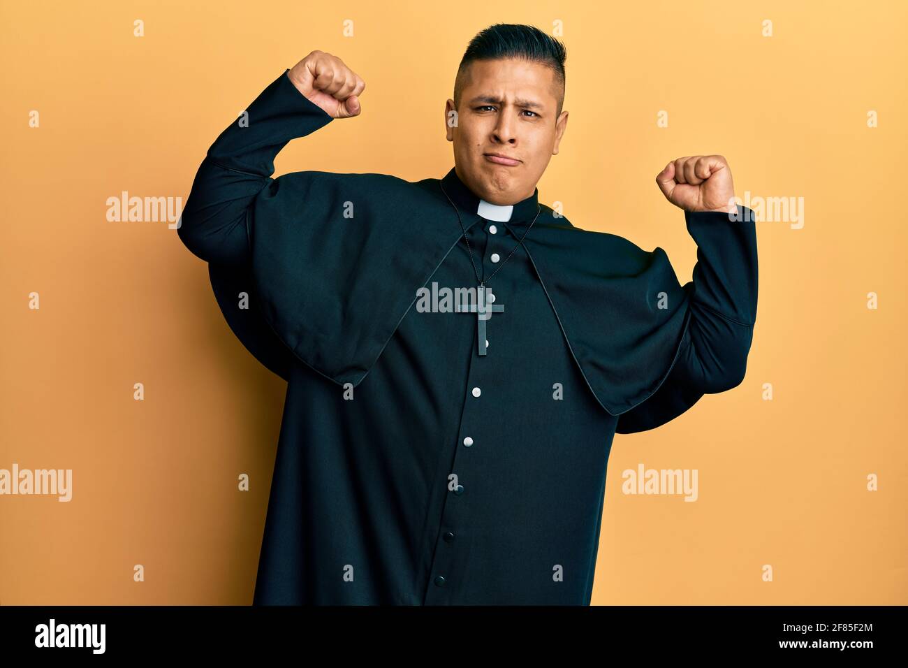Young latin priest man standing over yellow background showing arms ...
