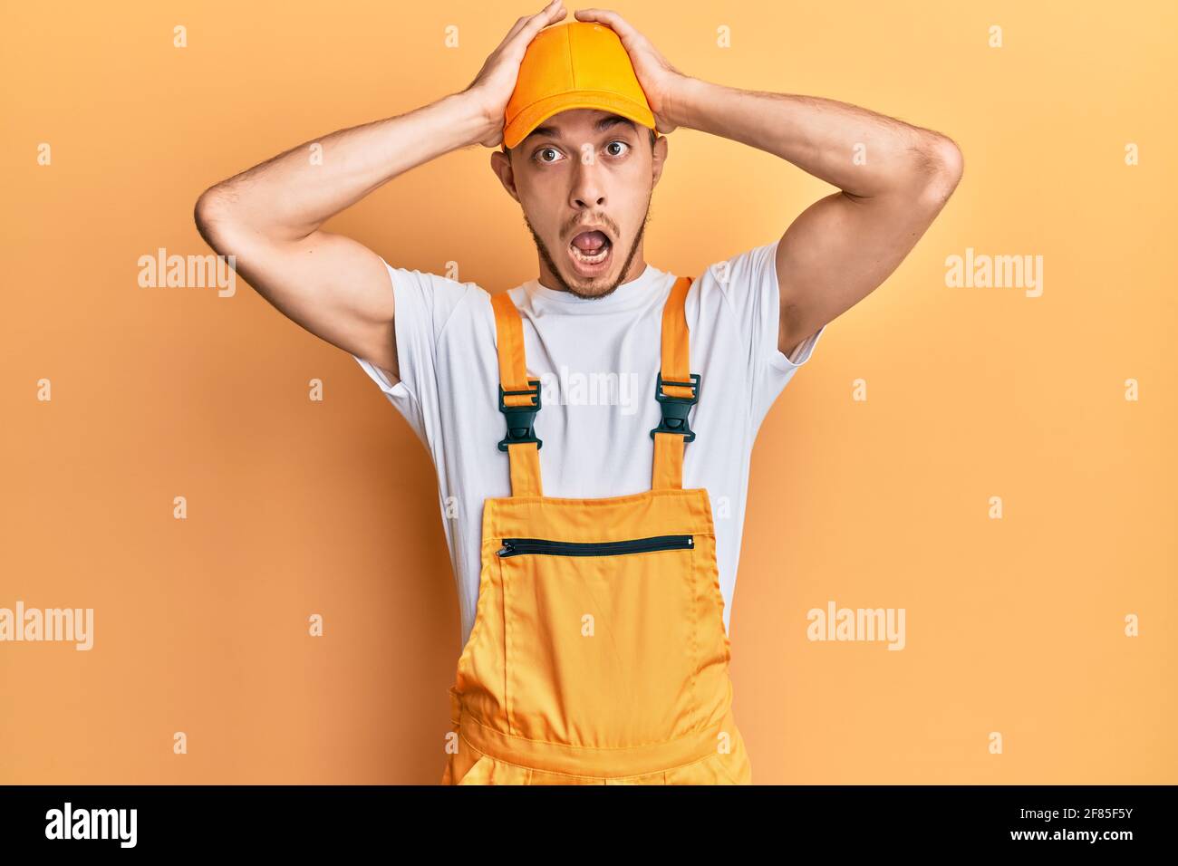 Hispanic young man wearing handyman uniform crazy and scared with hands ...