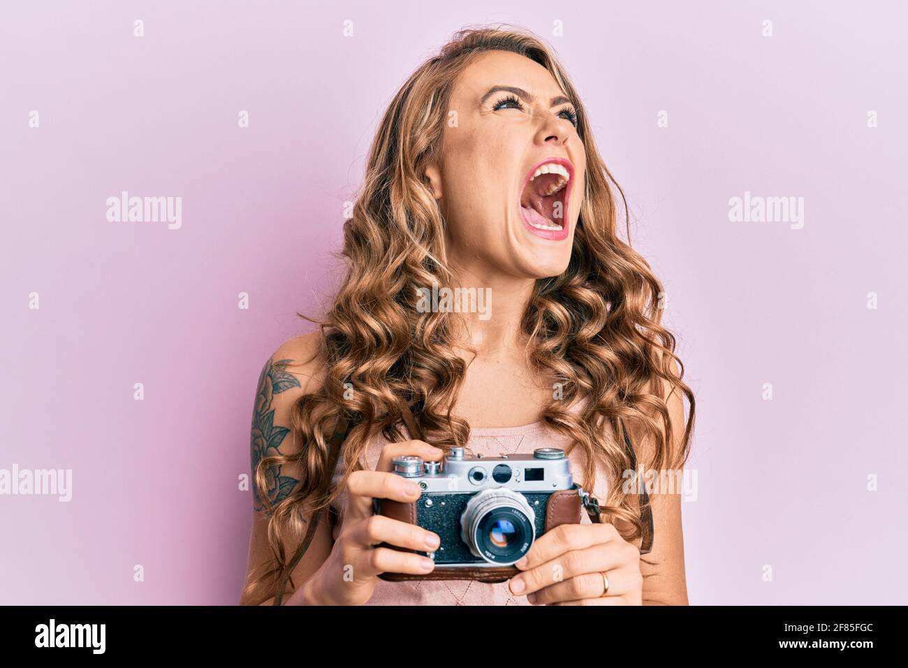 Young blonde girl holding vintage camera angry and mad screaming ...