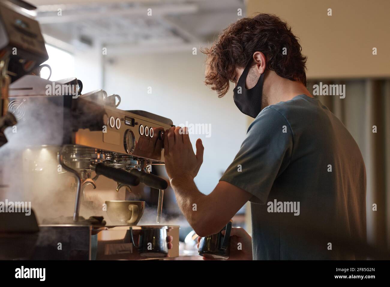 Side view portrait of young barista wearing mask while making fresh ...