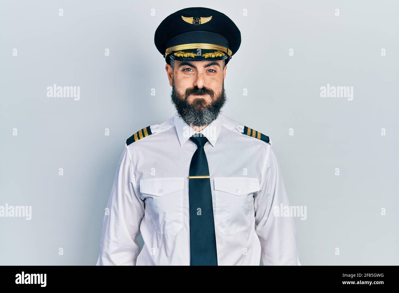 Young hispanic man wearing airplane pilot uniform puffing cheeks with ...