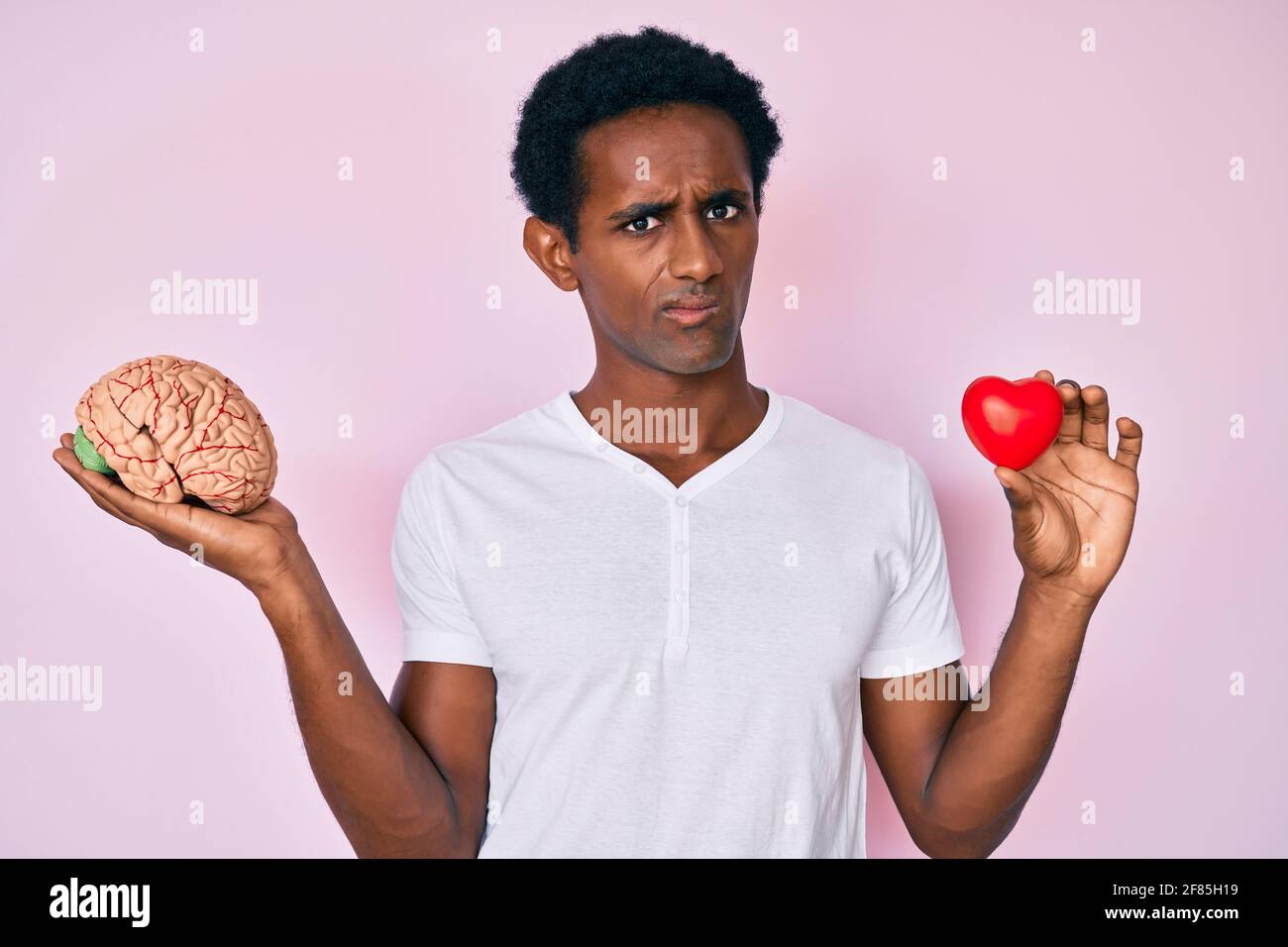 Handsome african man holding brain and heart clueless and confused ...