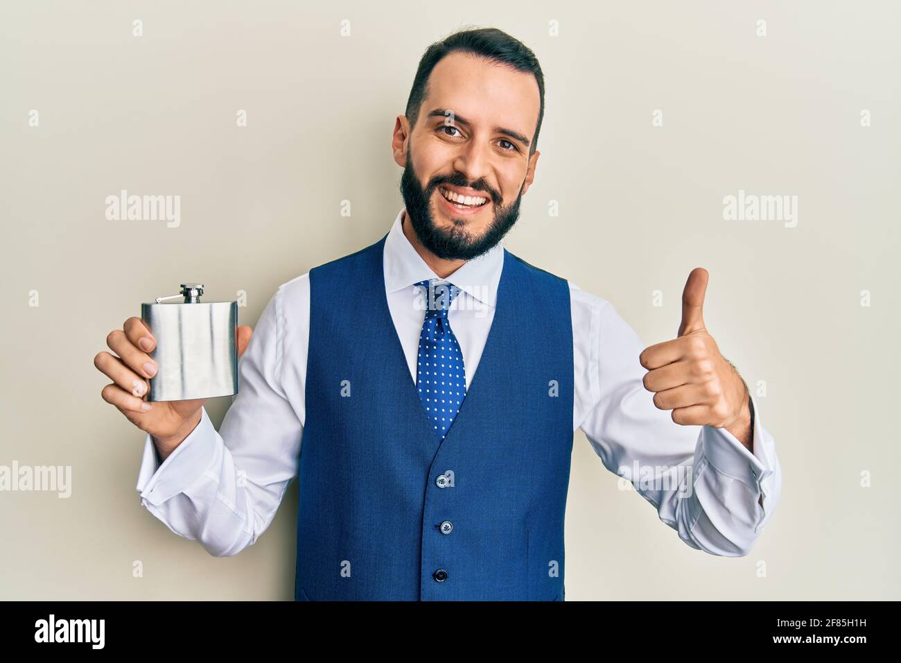 Young man with beard drinking whiskey from flask smiling happy and ...