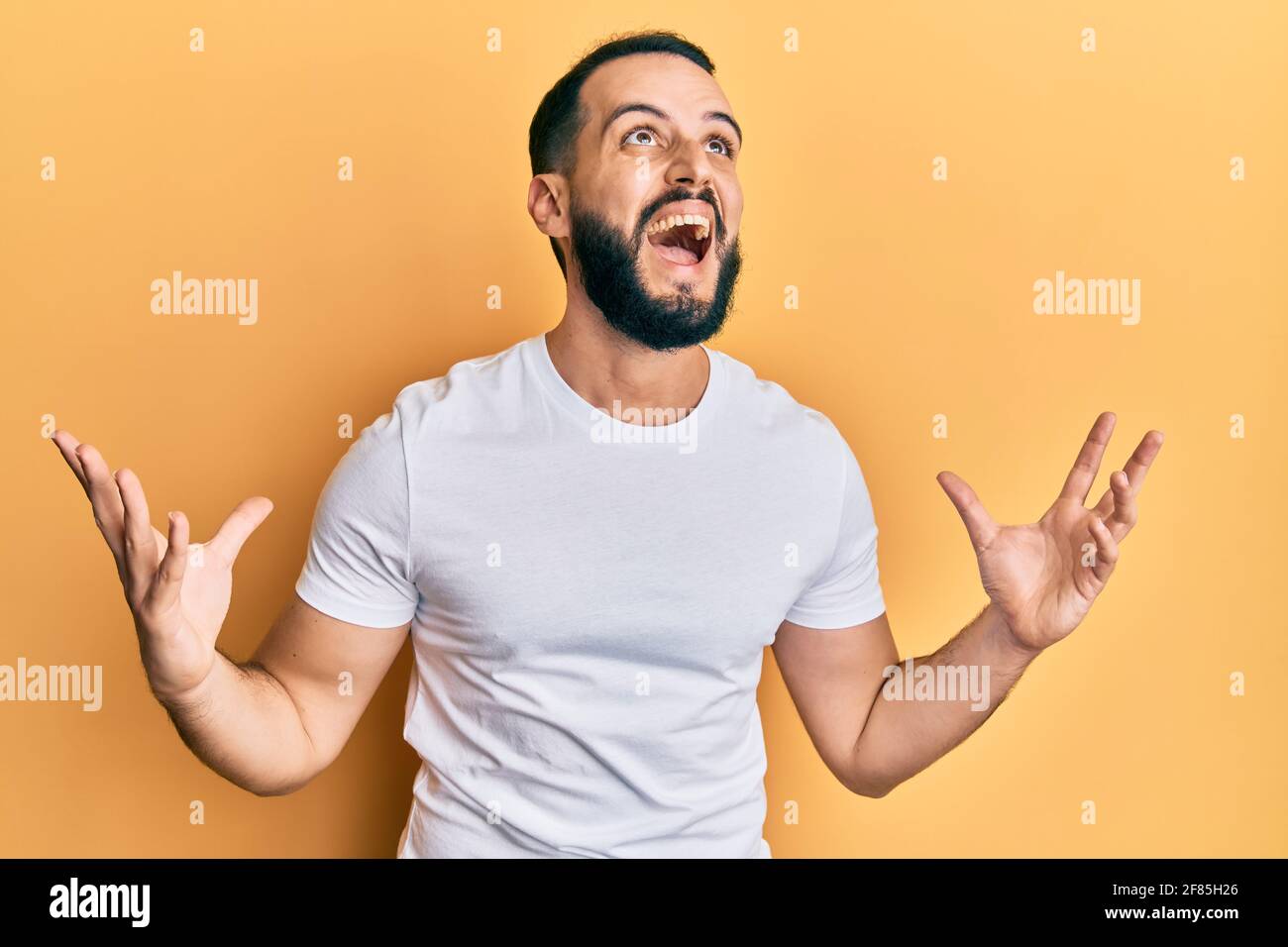 Young man with beard wearing casual white t shirt crazy and mad ...