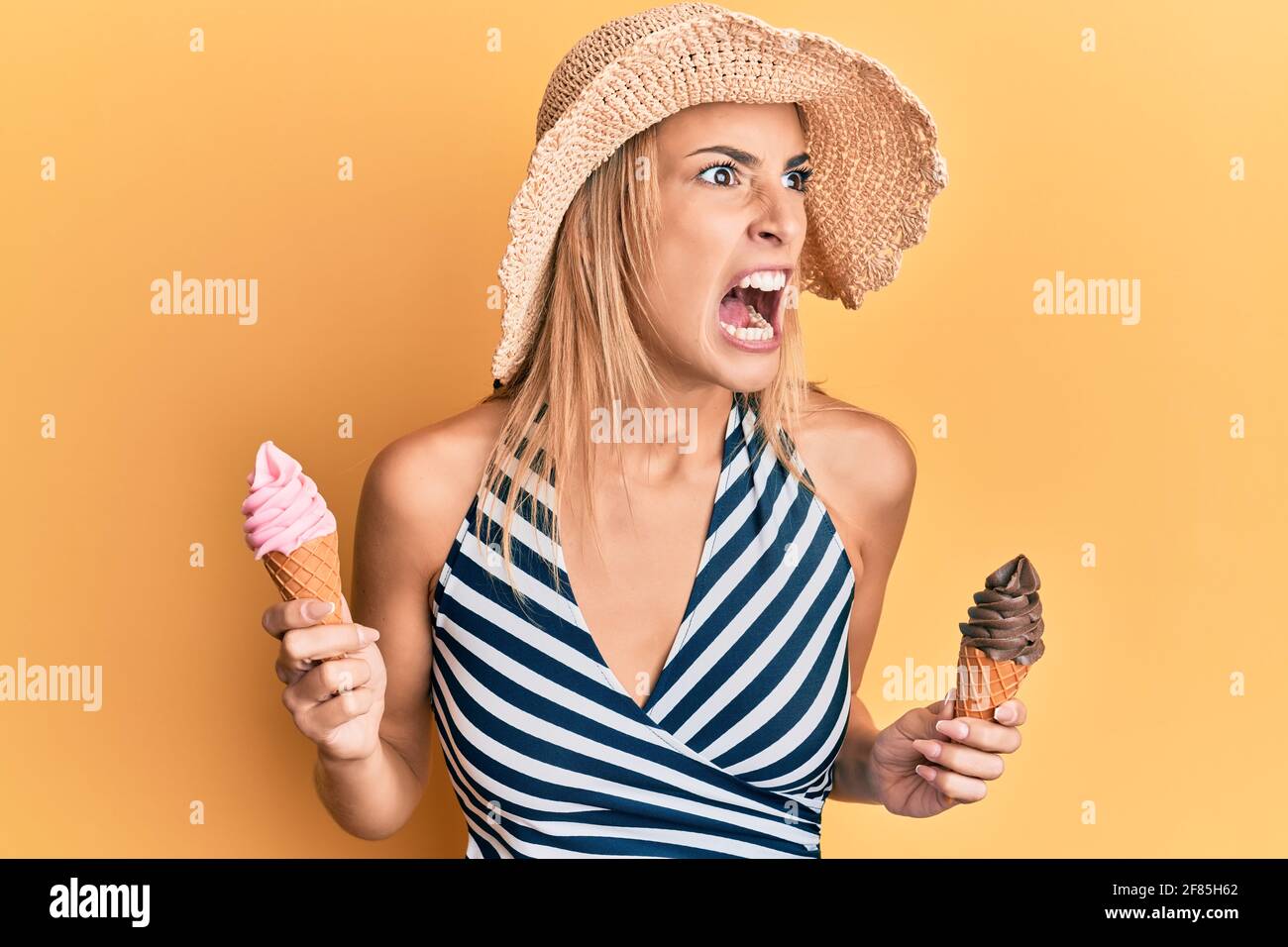 Beautiful blonde woman wearing summer style holding ice cream angry and ...
