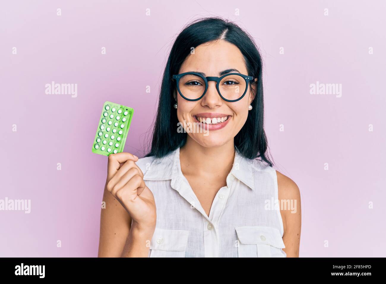 Beautiful young woman holding birth control pills looking positive and ...