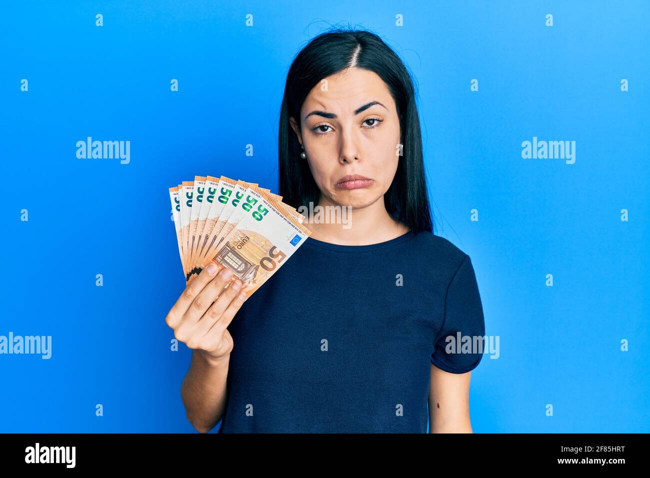 Beautiful young woman holding bunch of 50 euro banknotes depressed and ...