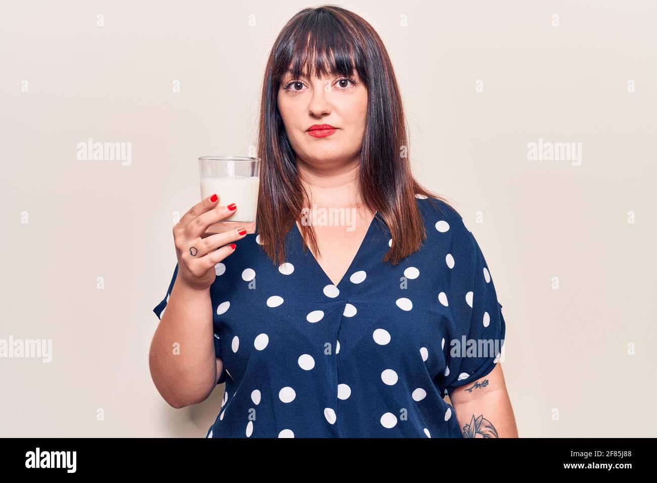 Young plus size woman holding glass of milk thinking attitude and sober ...