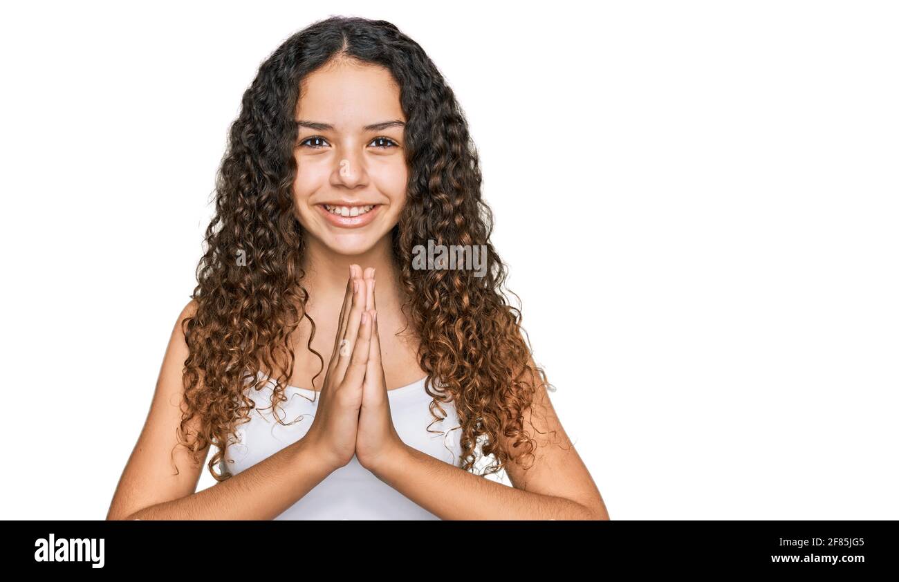 Teenager hispanic girl wearing casual clothes praying with hands ...