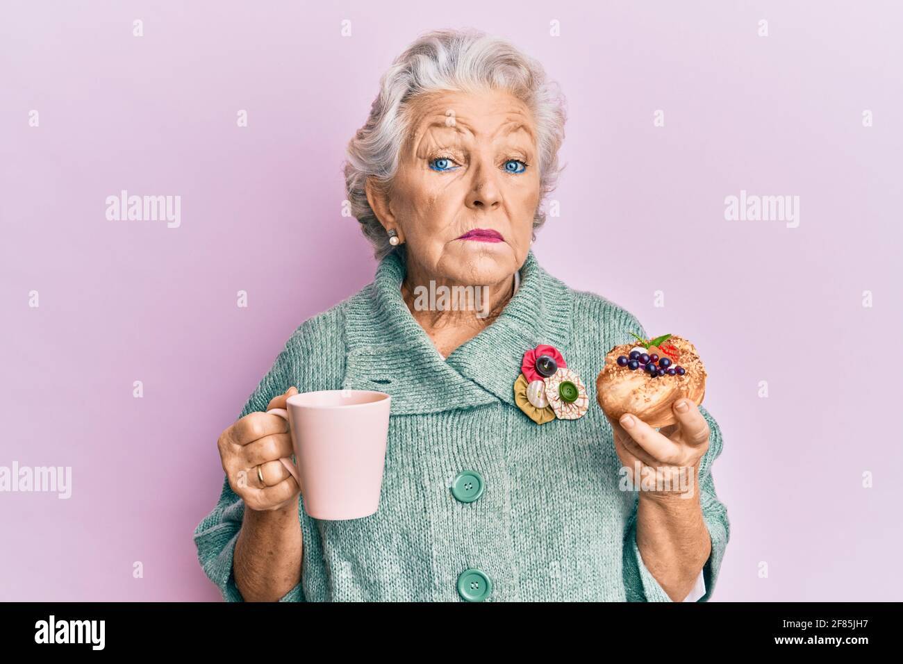 Senior grey-haired woman drinking a cup of coffee and eating bun ...