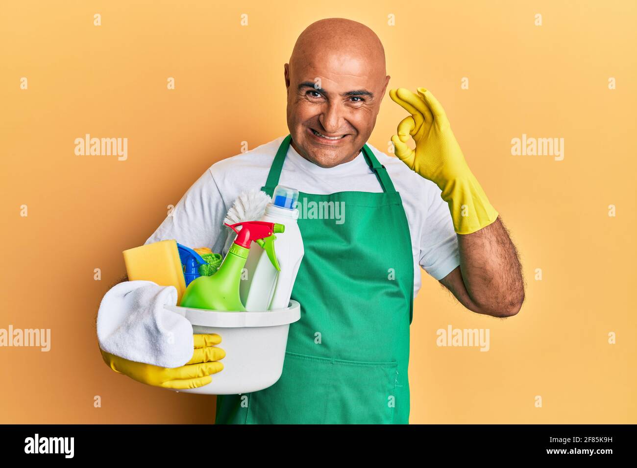 Mature middle east man wearing cleaner apron holding cleaning products ...