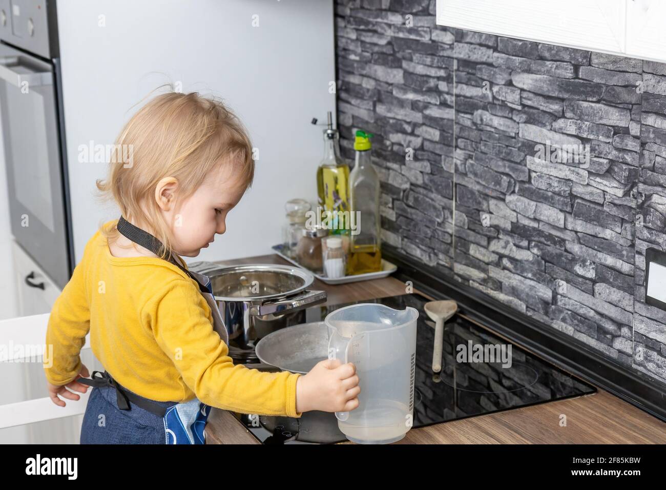 Cute little boy is holding a measuring cup for water in the kitchen ...