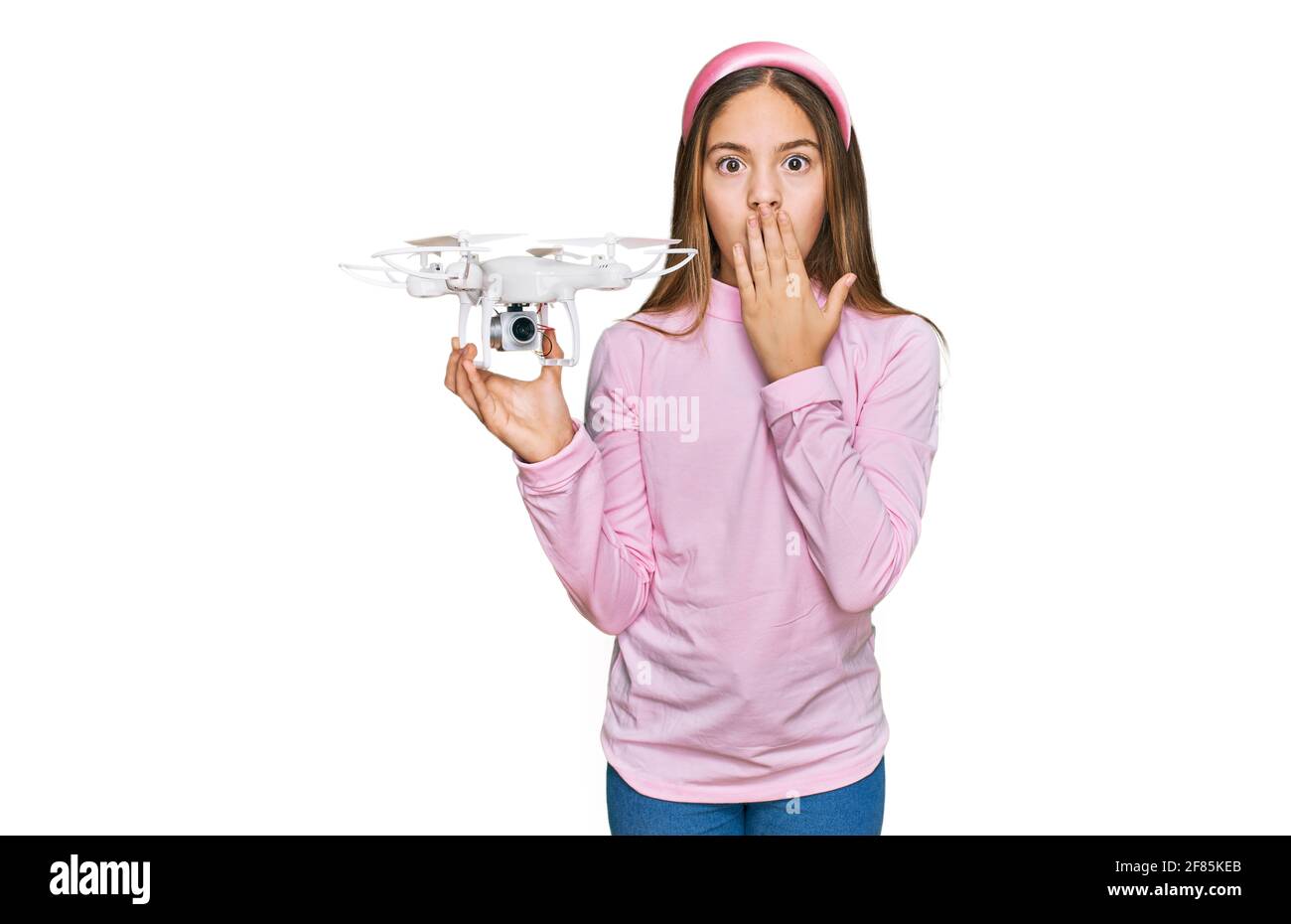 Beautiful brunette little girl using drone covering mouth with hand ...