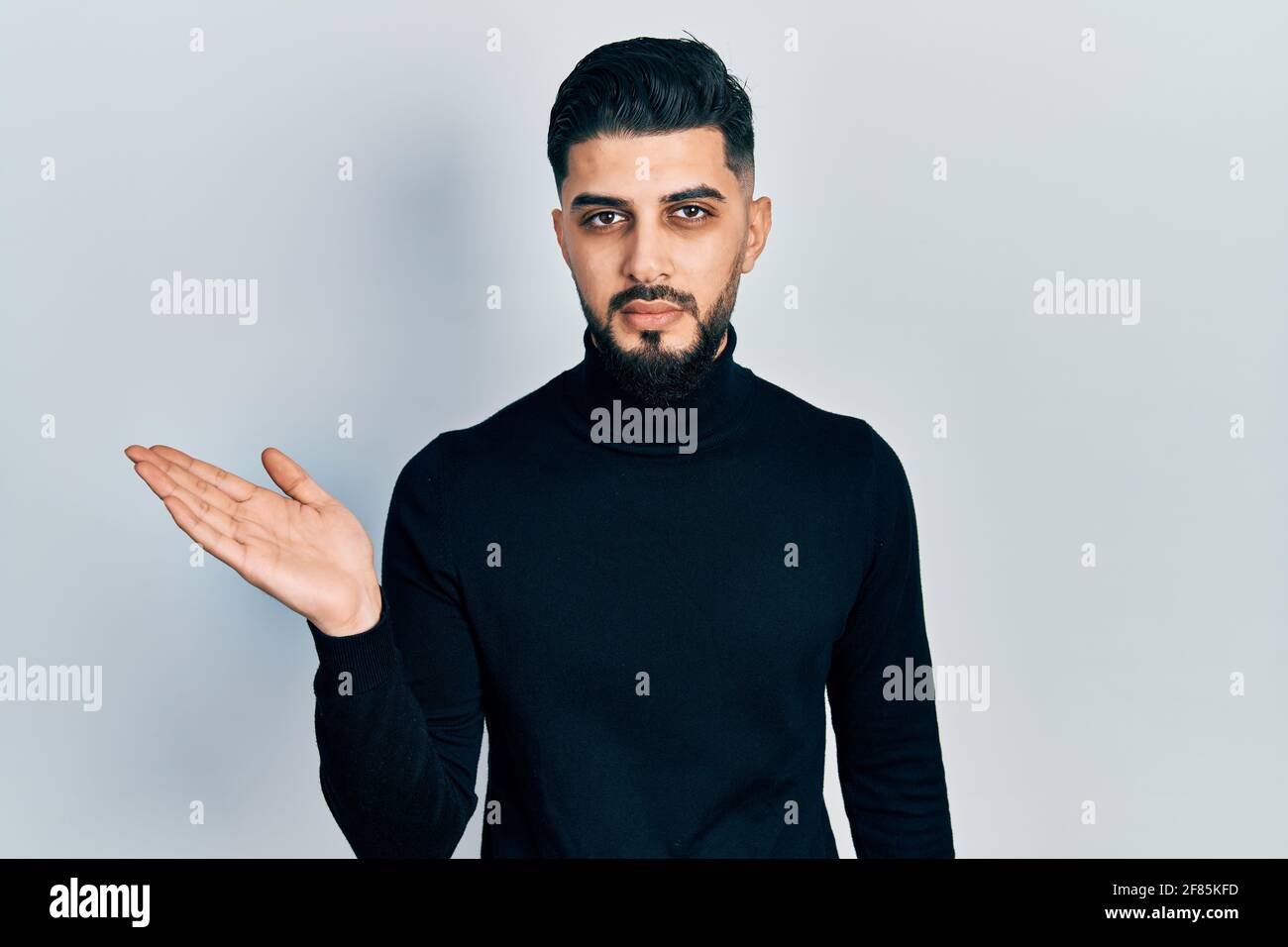 Handsome man with beard presenting with open palm relaxed with serious ...