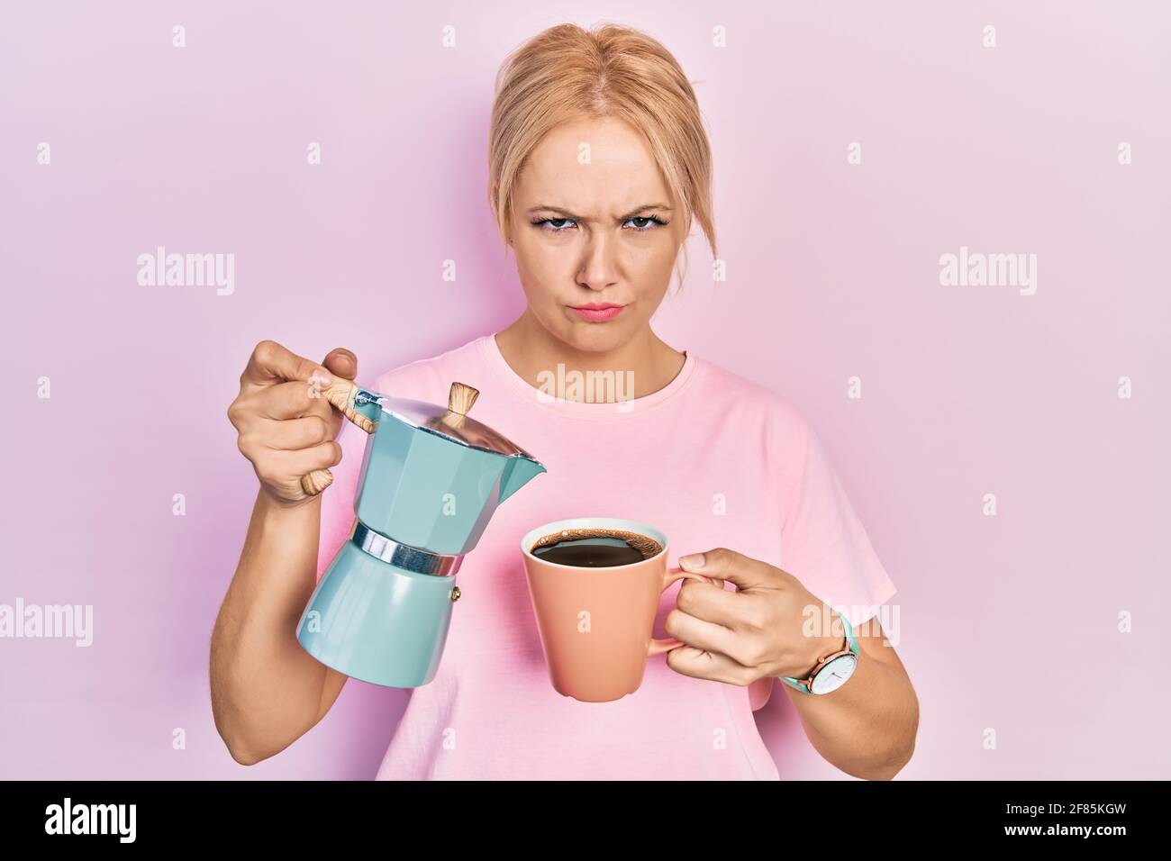 Young blonde woman drinking a cup fresh coffee skeptic and nervous ...