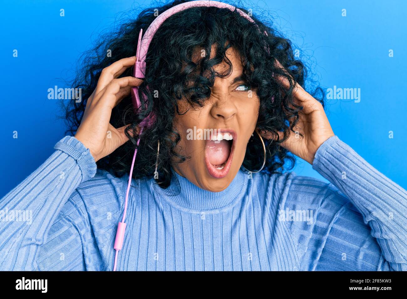 Young hispanic woman listening to music using headphones angry and mad ...