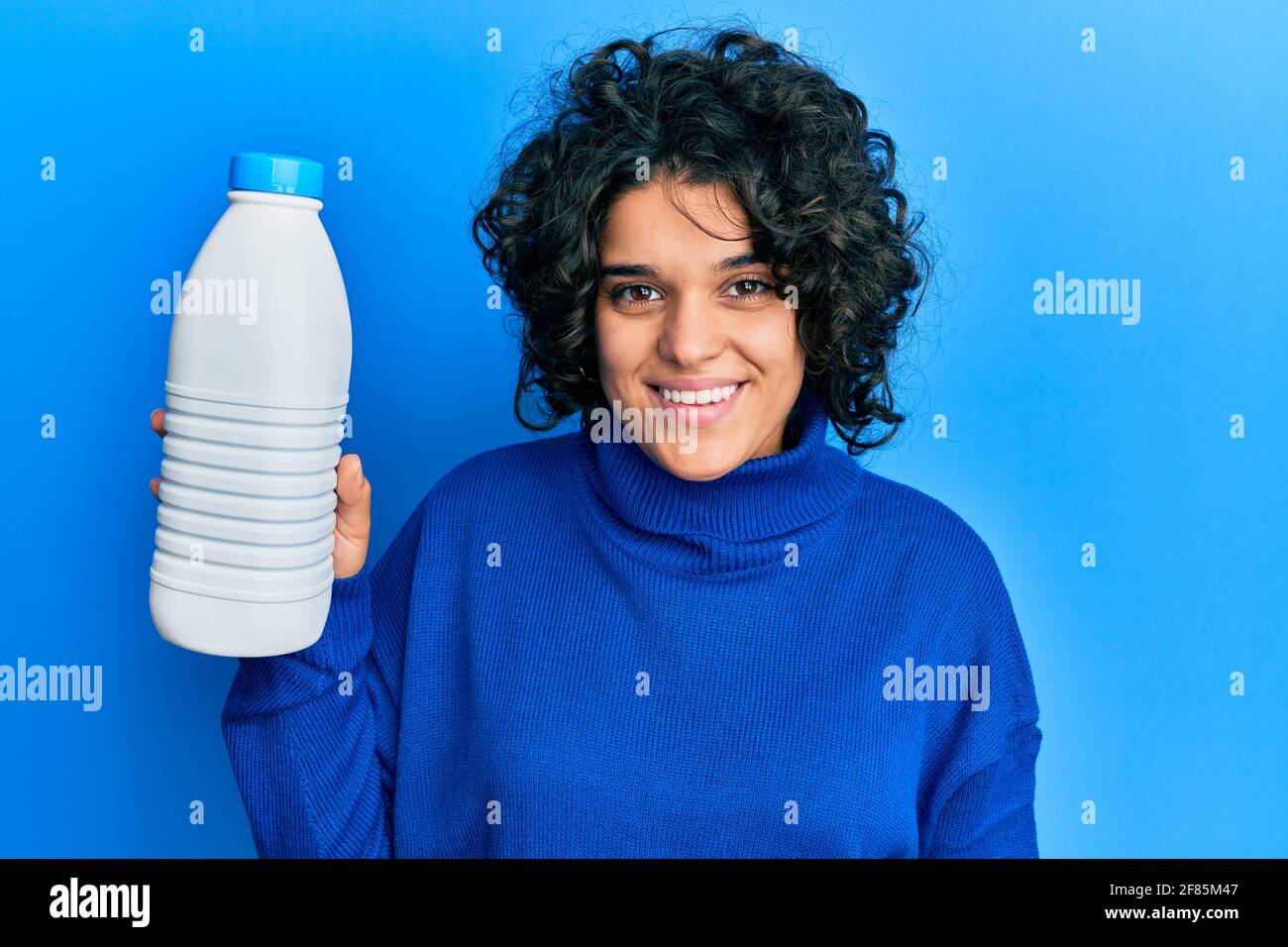 Young hispanic woman with curly hair holding liter bottle of milk ...