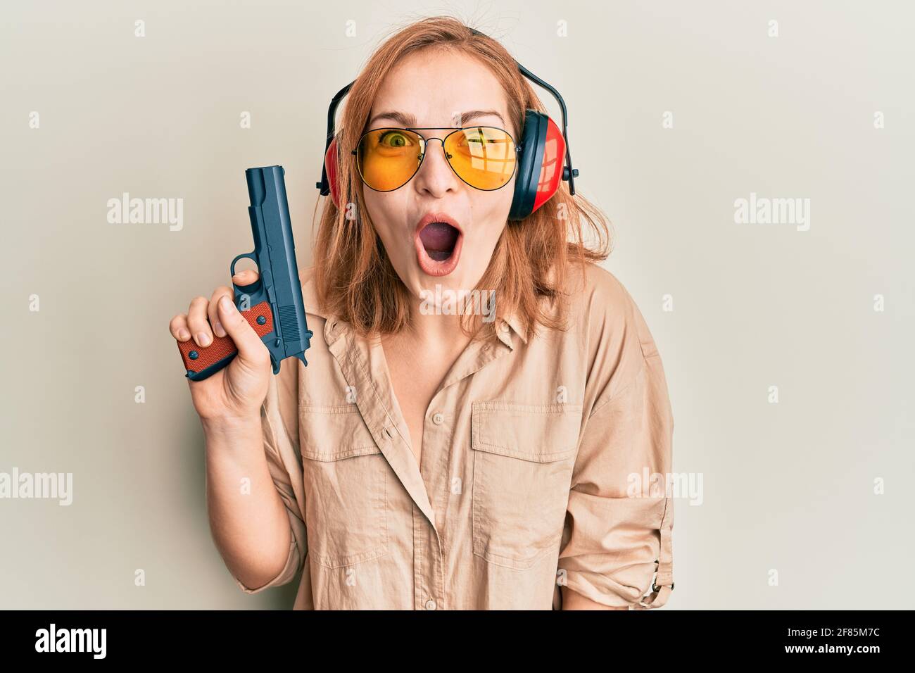 Young caucasian shooter woman using gun scared and amazed with open ...