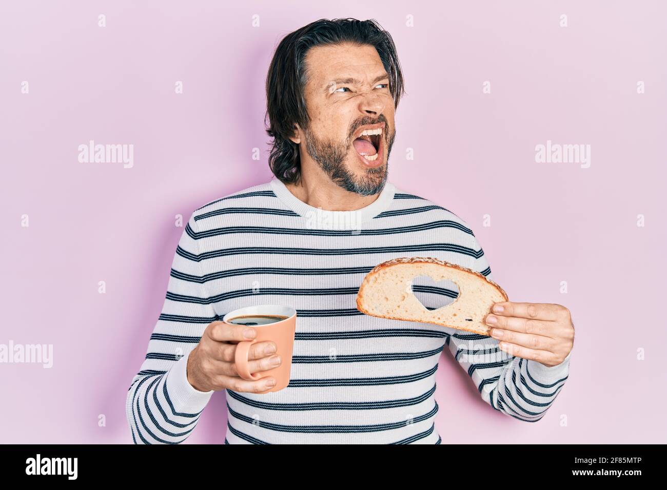 Middle age caucasian man holding bread loaf with heart shape drinking ...