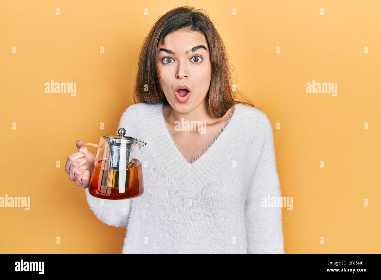 Young caucasian girl holding jar of tea scared and amazed with open ...