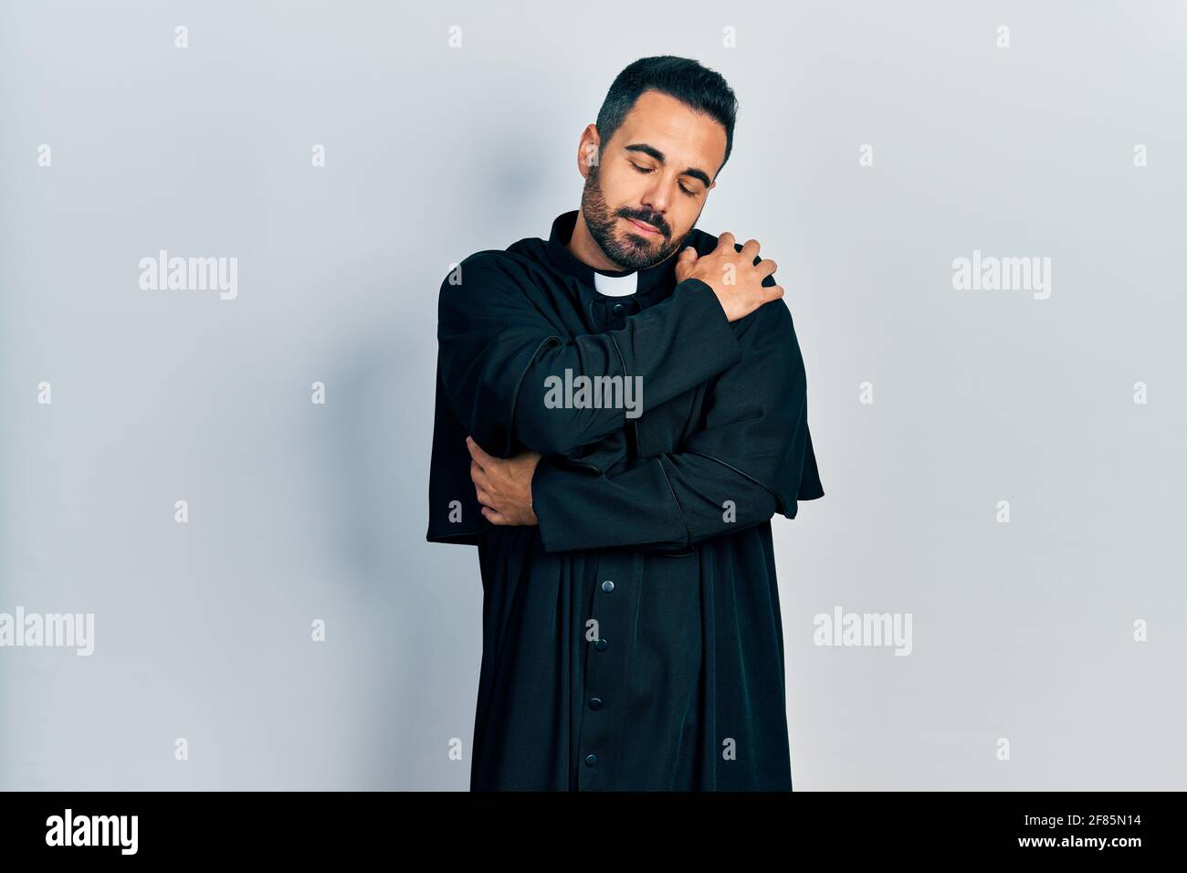 Handsome hispanic man with beard wearing catholic priest robe hugging ...