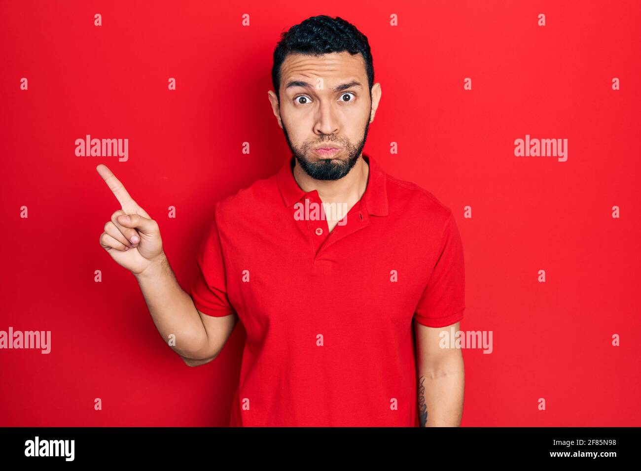 Hispanic man with beard pointing with fingers to the side puffing ...