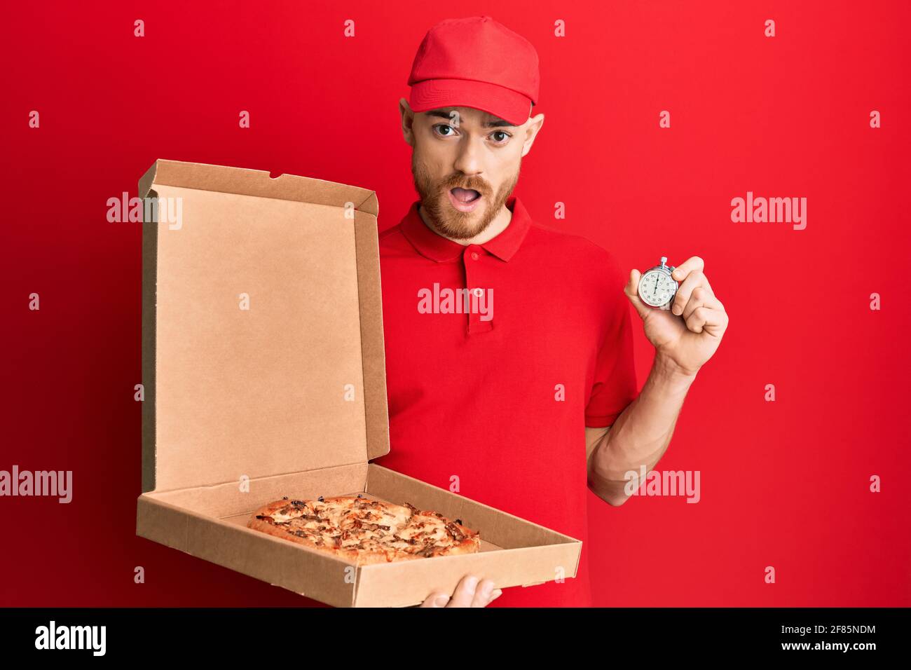 Young redhead man wearing delivery uniform holding pizza box and ...