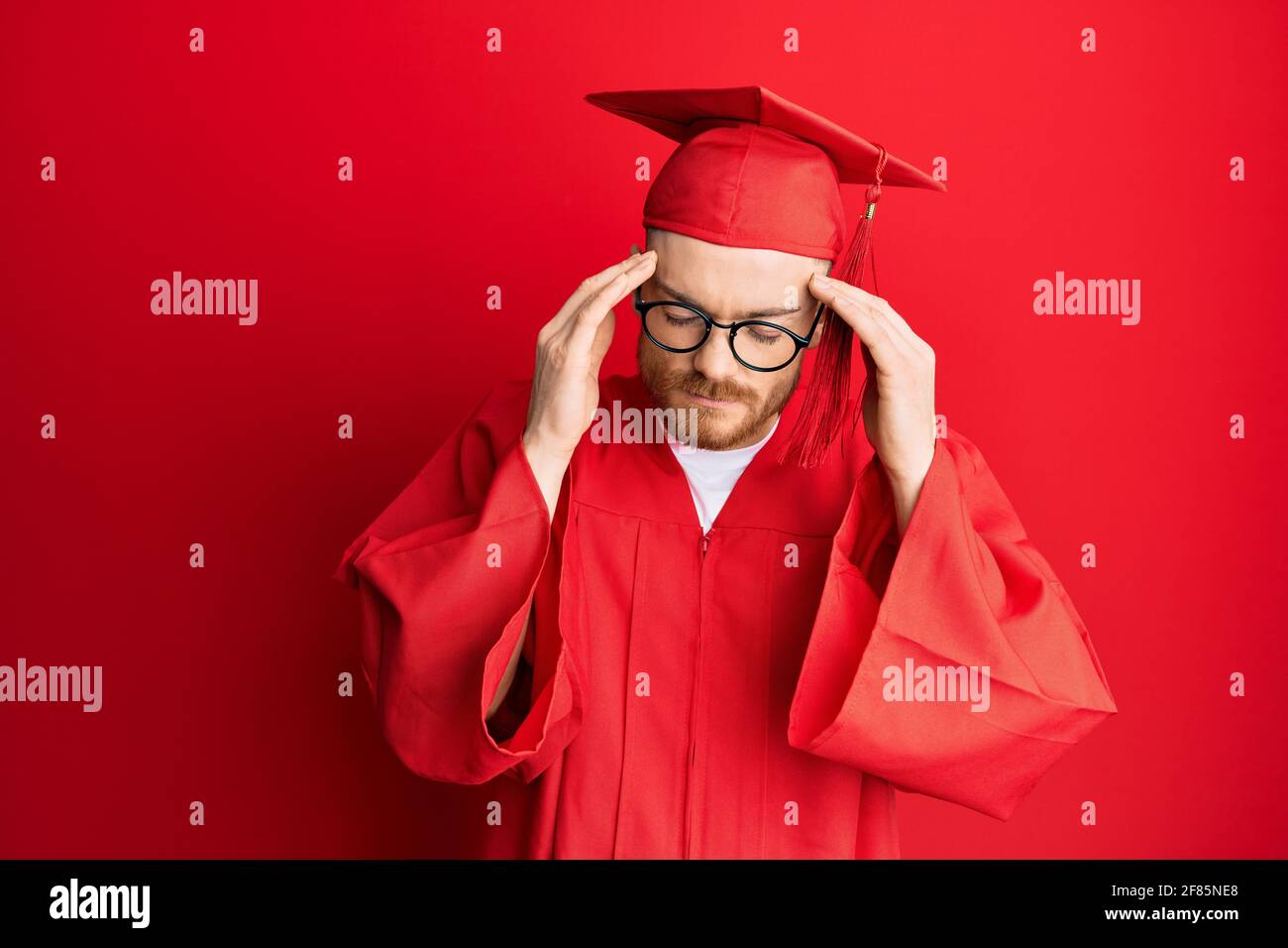 Young redhead man wearing red graduation cap and ceremony robe with ...