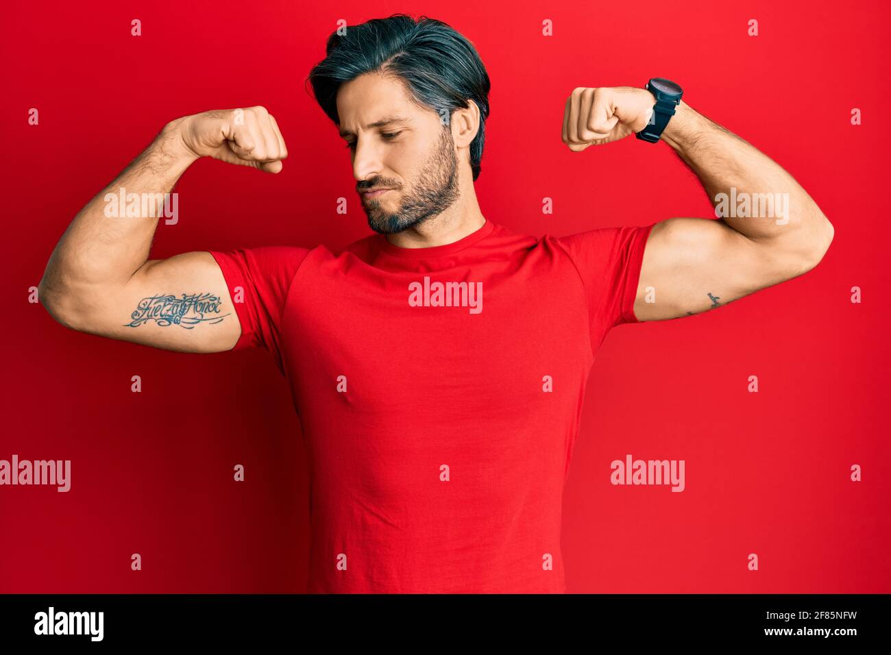 Young hispanic man wearing casual red t shirt showing arms muscles ...