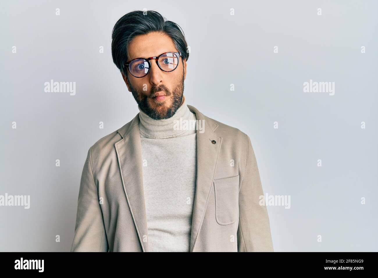 Young hispanic man wearing business jacket and glasses making fish face ...