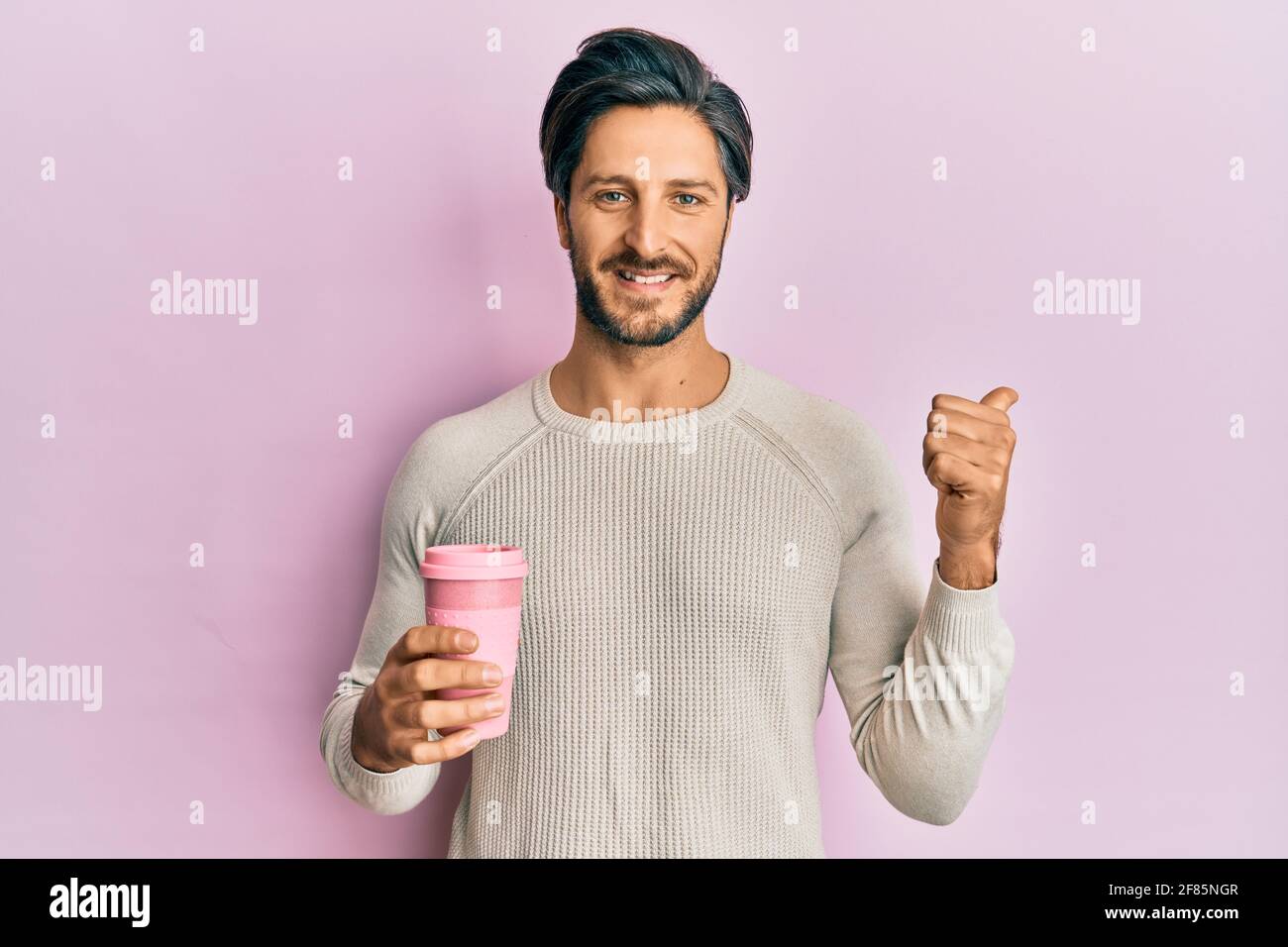 Young hispanic man drinking a take away cup of coffee pointing thumb up ...