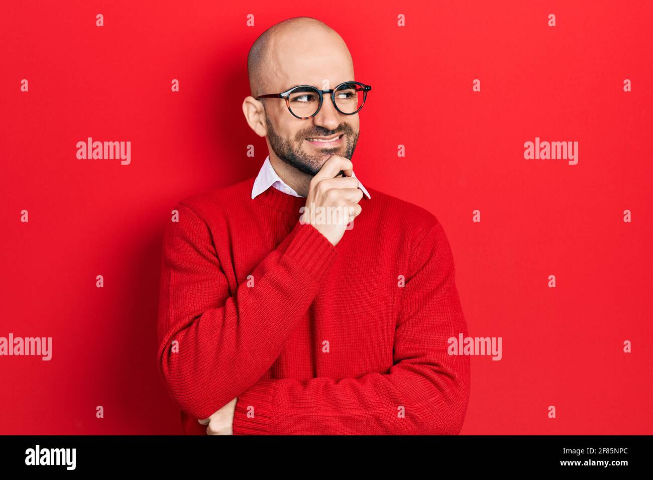 Young bald man wearing casual clothes and glasses with hand on chin ...